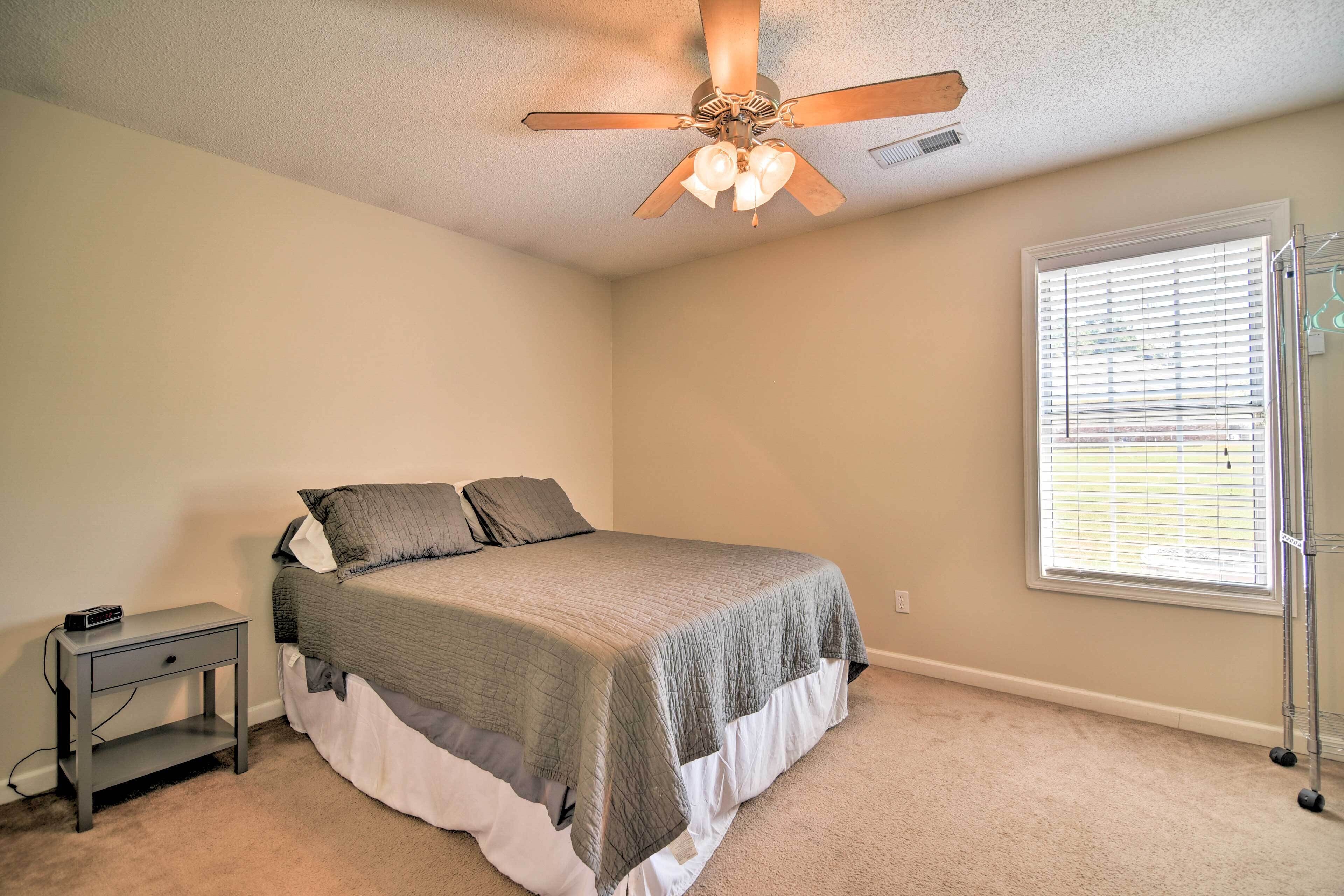 Quarto com cama, mesa de cabeceira, ventilador de teto, janela com persianas e radiador.