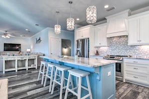 Uma cozinha moderna com armários brancos, uma ilha azul com banquetas, eletrodomésticos de aço inoxidável e azulejos decorativos na parede.