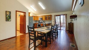 Uma ampla sala de jantar com uma mesa e cadeiras de madeira, uma cozinha com armários de madeira e vista para o exterior.