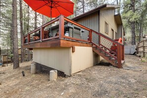 Uma cabana com deck de madeira, escadas e um guarda-chuva vermelho.
