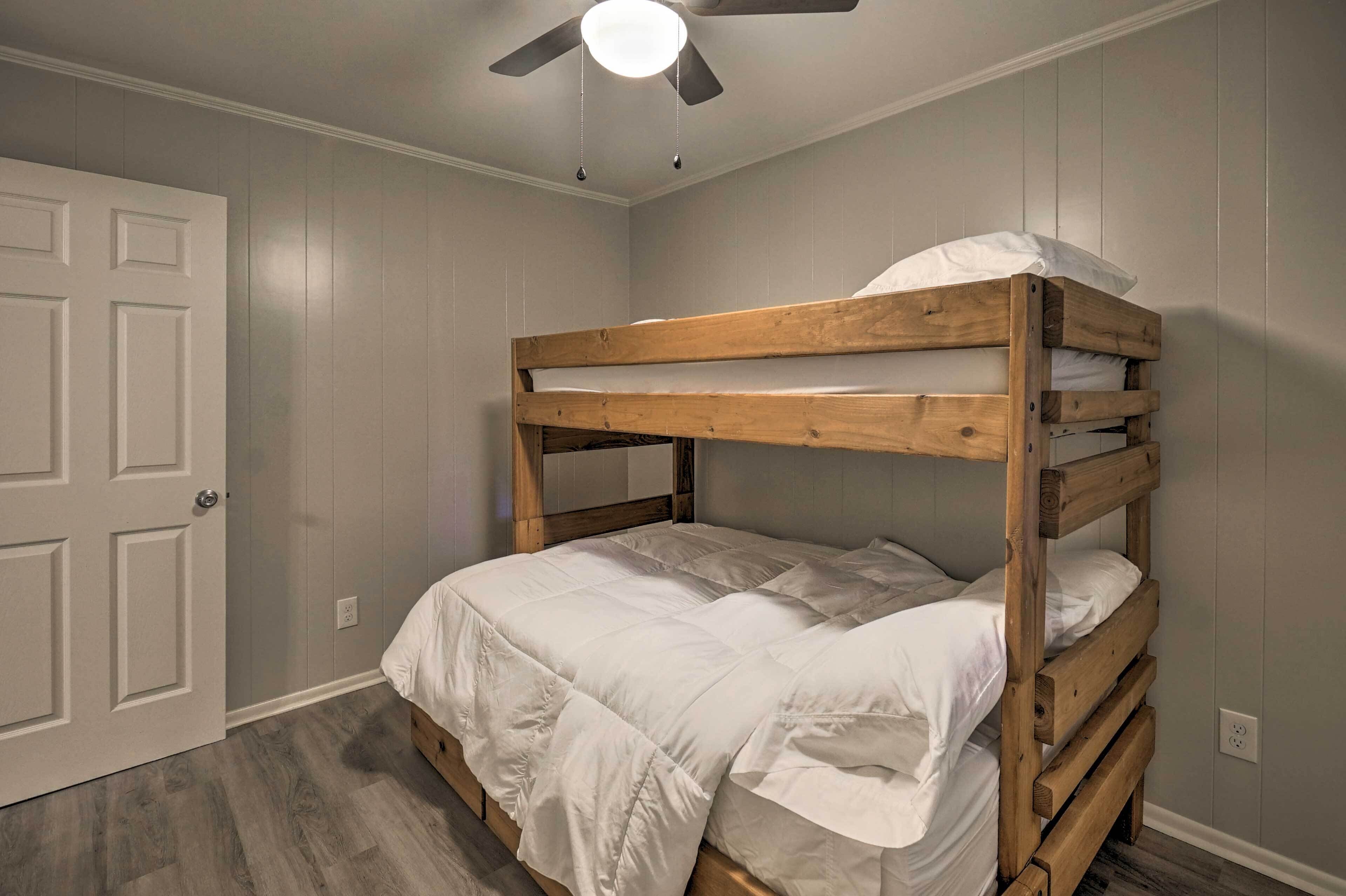 Uma cama beliche com roupa de cama branca em um quarto com paredes cinza claro e um ventilador de teto.