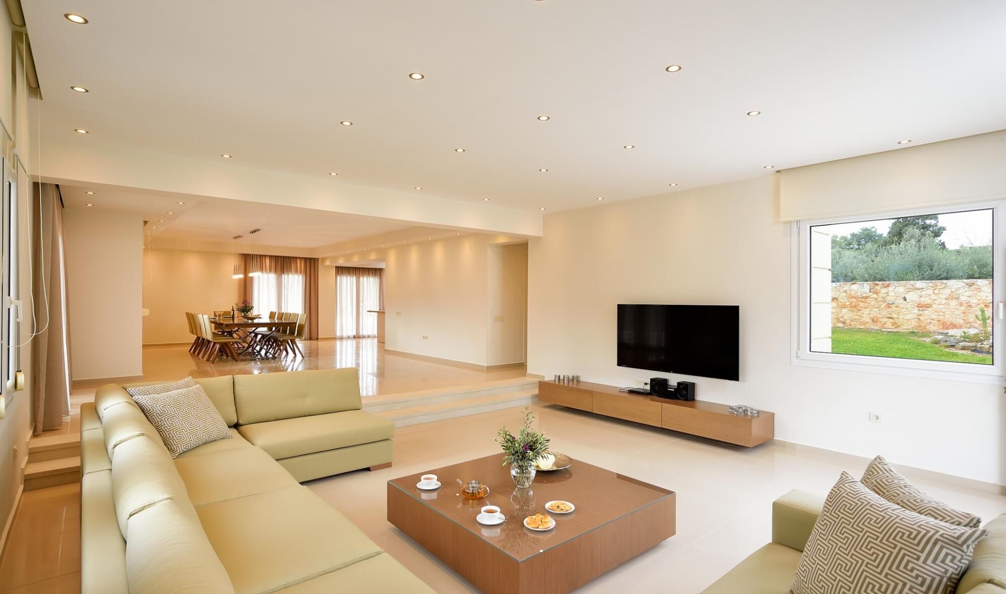 Uma sala de estar moderna com sofá, mesa de centro, TV e uma área de jantar ao fundo.