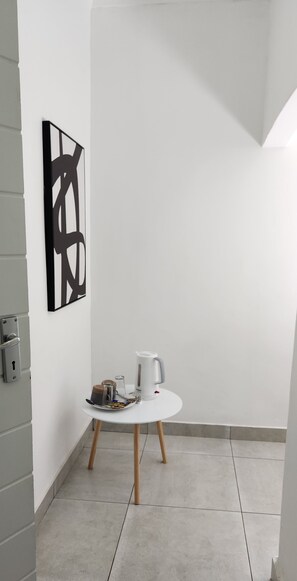 Quarto minimalista com uma mesa branca, uma cafeteira e uma obra de arte abstrata emoldurada na parede.