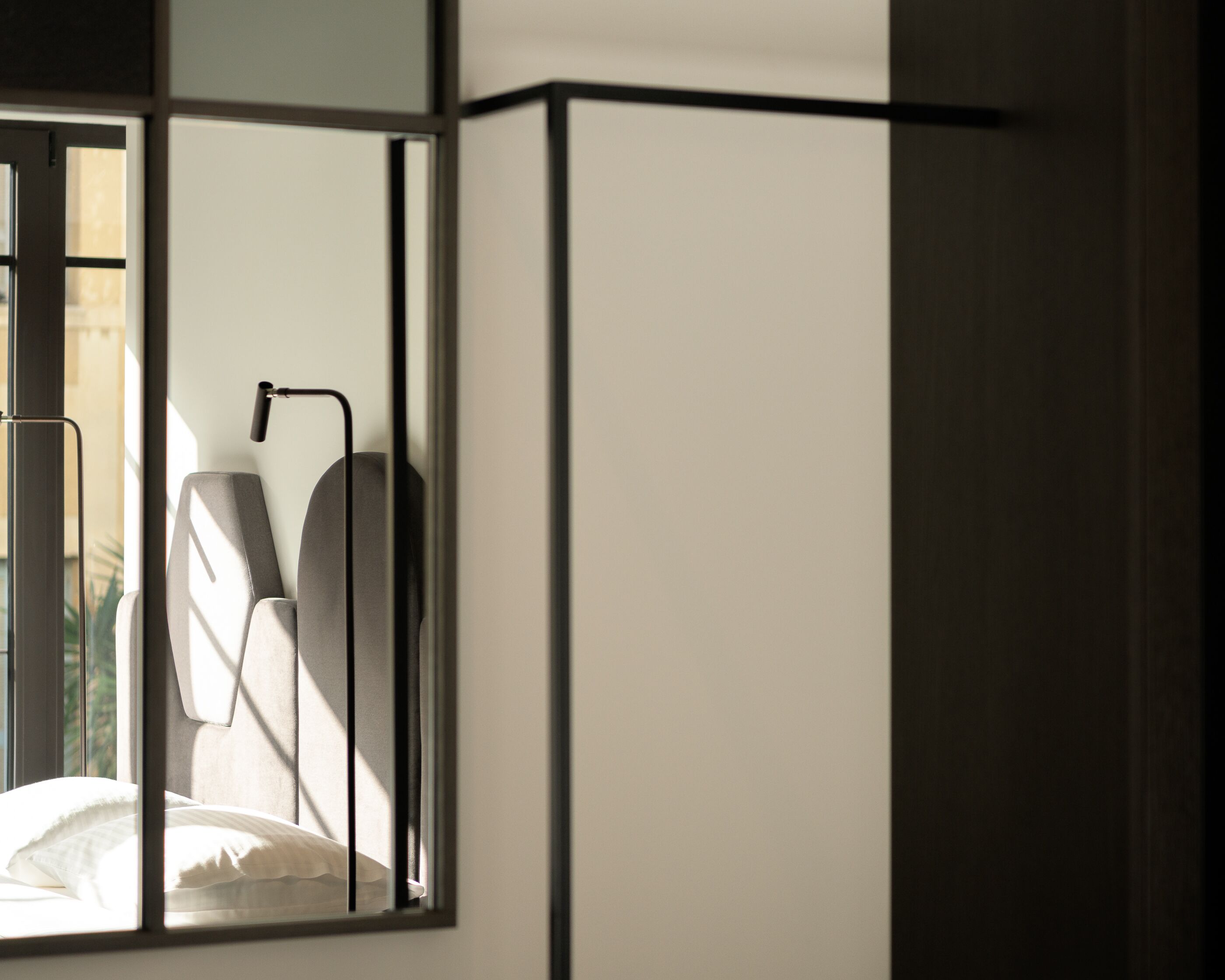 Quarto moderno com cama, mesa de cabeceira e espelho refletindo a vista da janela.