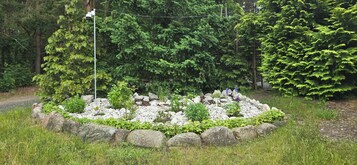 Um jardim com um canteiro de pedras circulares, diversas plantas e uma cerca de madeira.