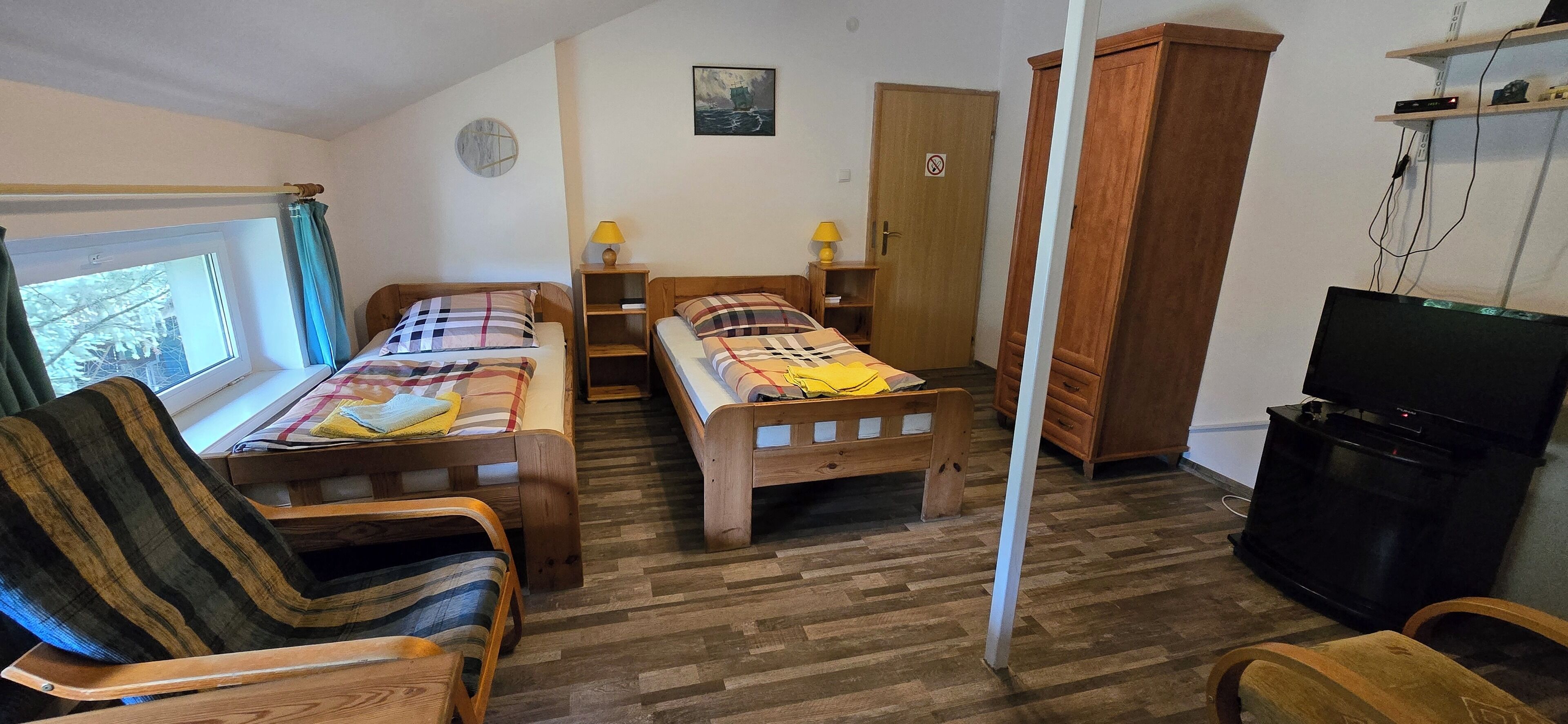 Quarto com duas camas de madeira, uma cadeira de madeira, televisão e guarda-roupa.