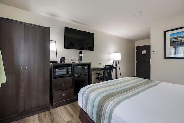 Quarto de hotel com cama, escrivaninha, TV de tela plana, guarda-roupa, micro-ondas e geladeira.