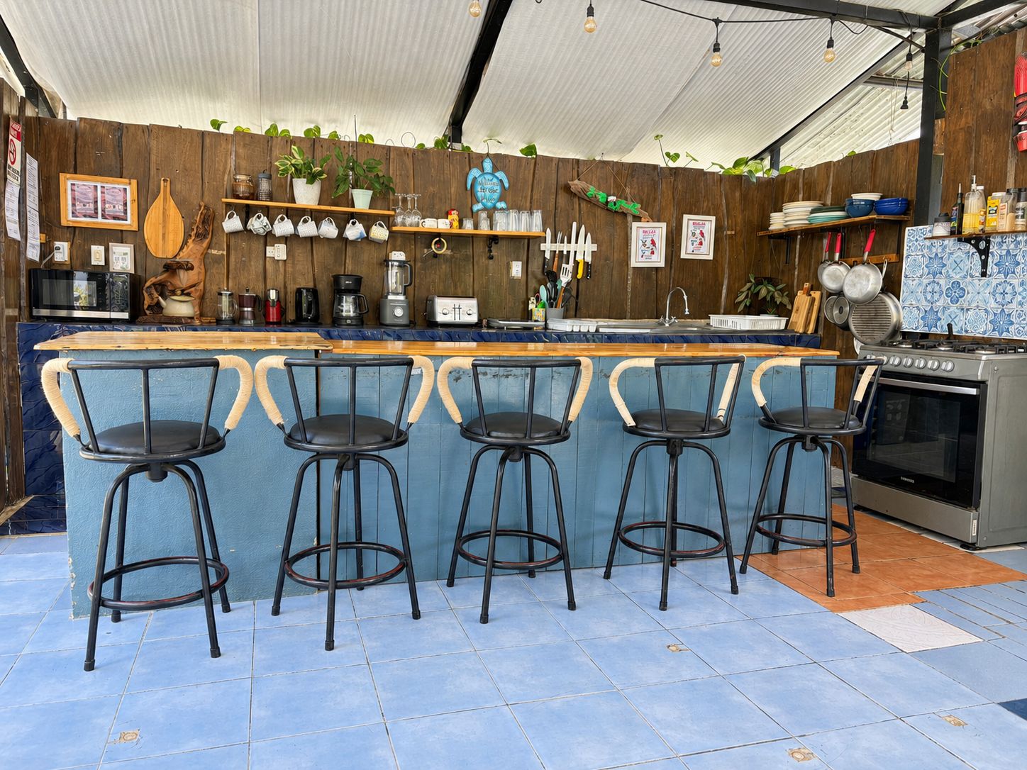 Uma área de bar com quatro banquetas, uma cozinha com fogão, e diversos utensílios de cozinha e decorações nas paredes.