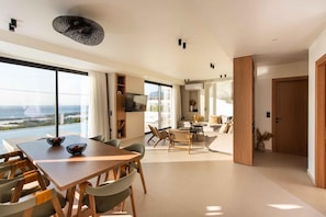 Uma sala de estar moderna com área de jantar, janelas amplas e vista para o oceano.