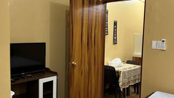 Quarto com guarda-roupa de madeira, televisão sobre um móvel, mesa de jantar com cadeiras e uma cama.