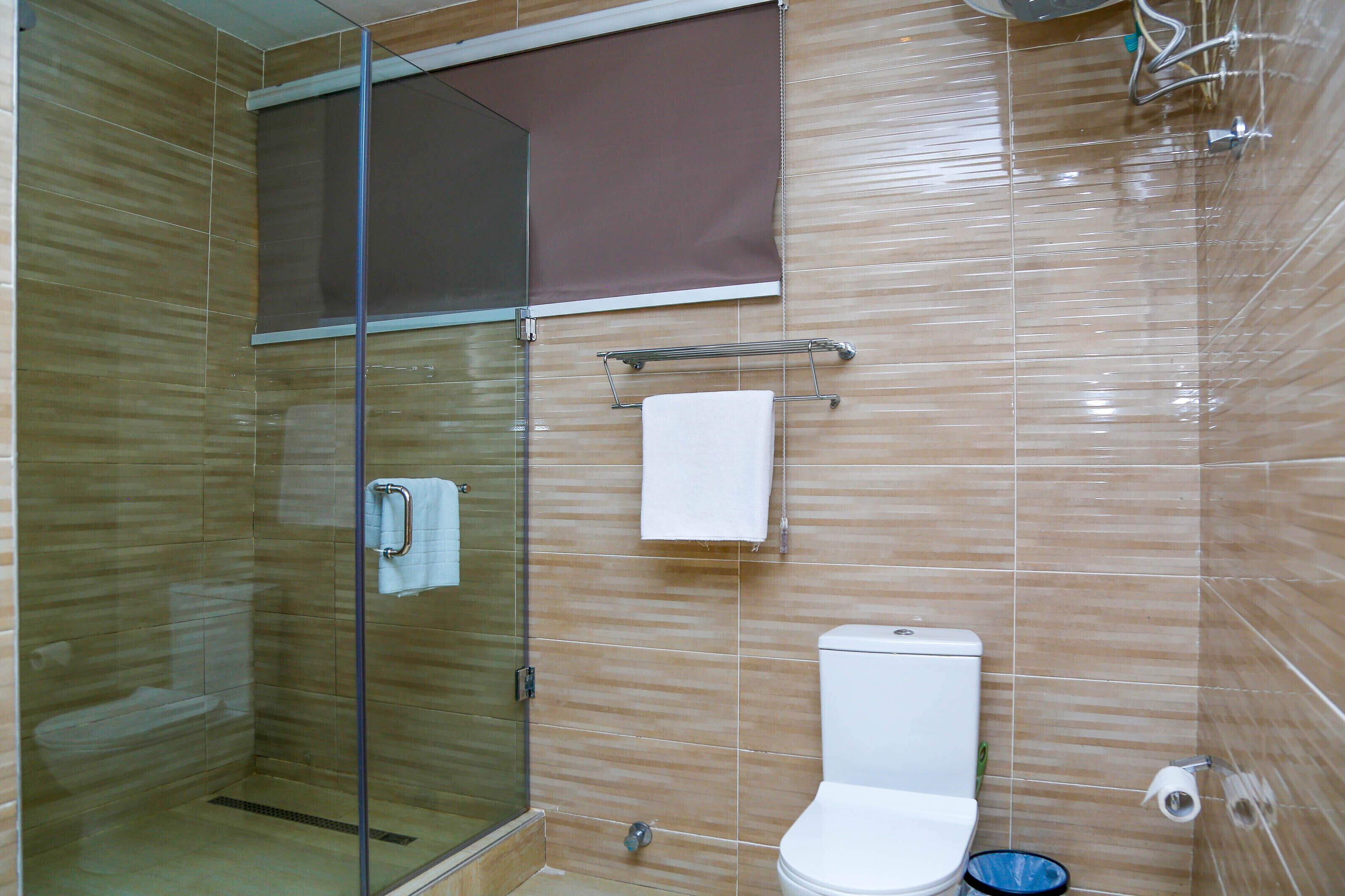 Casa de banho com cabine de duche em vidro, sanita e suporte para toalhas.