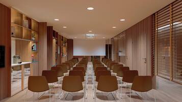 Uma sala de conferências com fileiras de cadeiras voltadas para uma tela central, painéis de madeira nas paredes e luminárias embutidas no teto.