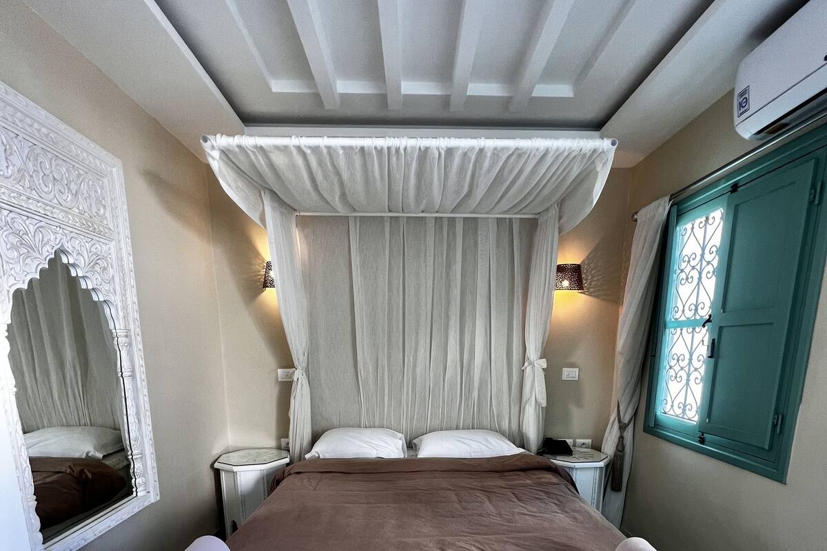 Quarto com uma cama grande, um sofá, um espelho e uma janela com cortinas.