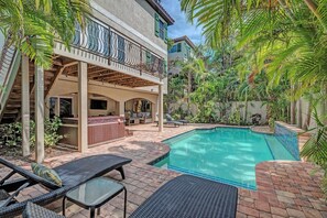 Uma área de piscina com espreguiçadeiras, uma banheira de hidromassagem e um terraço coberto com um bar.