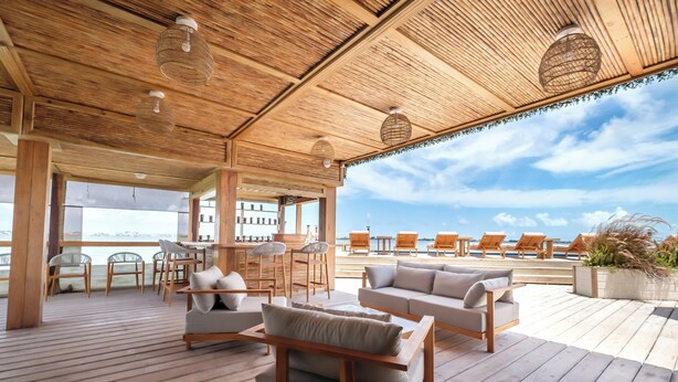 Um deck de madeira com área de estar ao ar livre, bar e vista para o oceano.