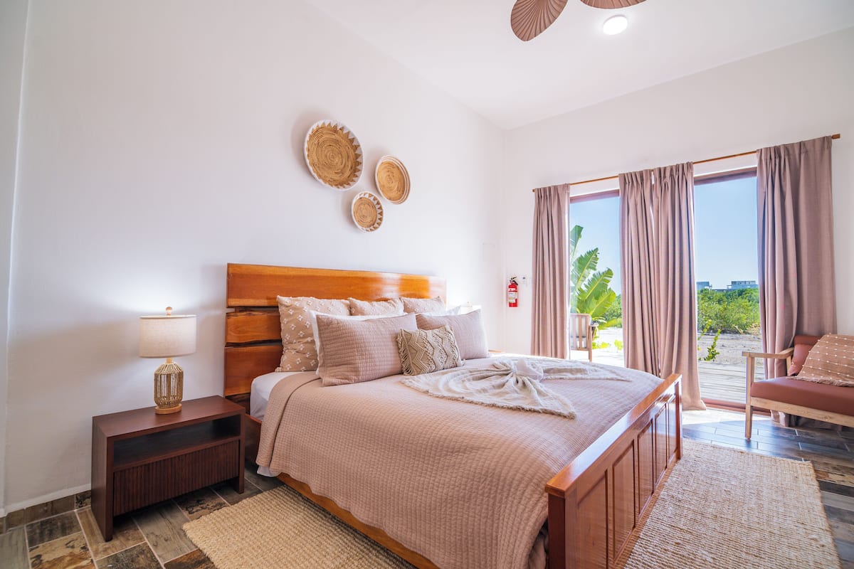 Quarto com cama, mesa de cabeceira, abajur e vista para o exterior.