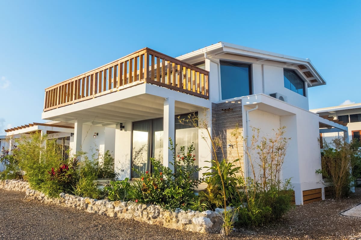 Uma casa moderna de dois andares com varanda, muro de pedra e jardim com diversas plantas.