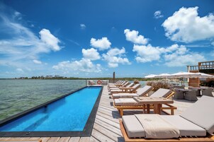 Área à beira da piscina com espreguiçadeiras e guarda-sóis, com vista para um corpo de água.