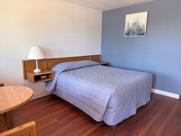 Quarto bem arrumado com cama, mesa de cabeceira, abajur e uma pequena mesa de madeira.
