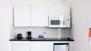 Uma cozinha compacta com armários brancos, micro-ondas, cafeteira e máquina de lavar louça.