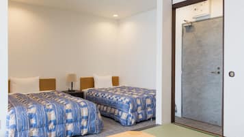 Quarto de hotel com duas camas, área de chuveiro e uma pequena mesa com abajur.