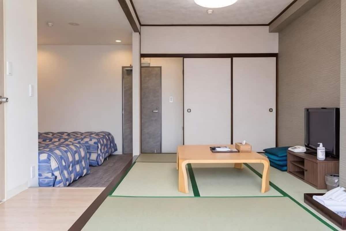 Um quarto com um futon, uma mesa de madeira, uma televisão e uma porta deslizante.