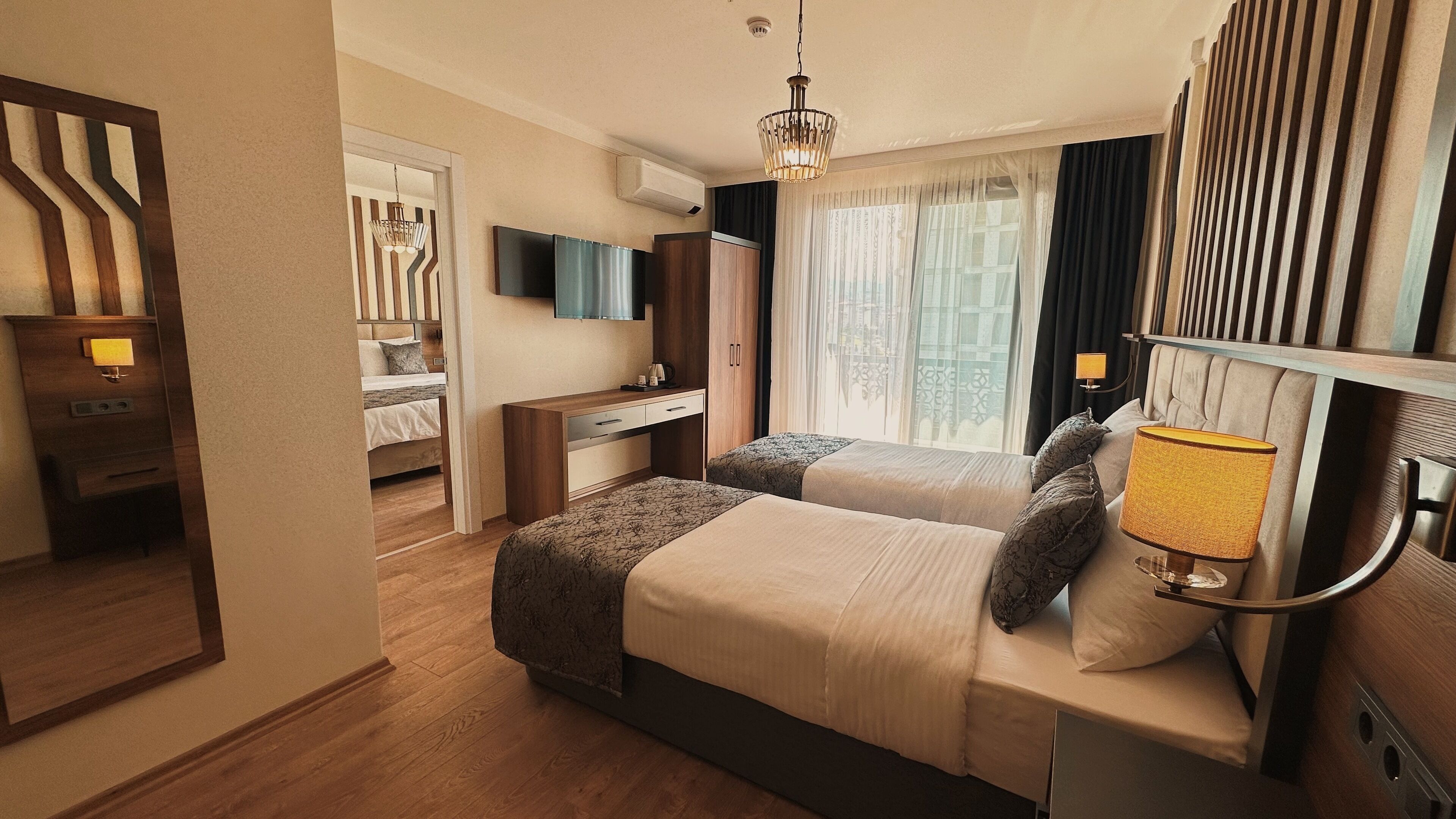 Quarto de hotel com duas camas, uma escrivaninha, uma TV e uma janela com cortinas.