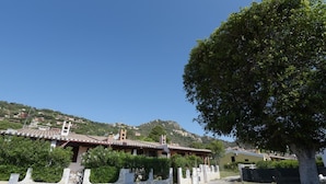 Um edifício residencial com telhado de cerâmica, rodeado por vegetação e colinas ao fundo.