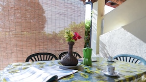 Uma mesa com toalha estampada, um vaso com flores, uma cafeteira verde e uma chávena sobre pires.
