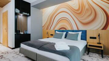 Quarto de hotel moderno com uma cama grande, um guarda-roupa de madeira, uma parede com um design abstrato e uma pequena mesa de cabeceira.