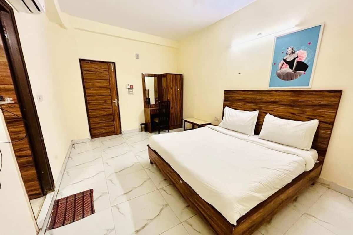 Quarto de hotel com cama de madeira, roupa de cama branca, piso de mármore, guarda-roupa de madeira e um quadro na parede.