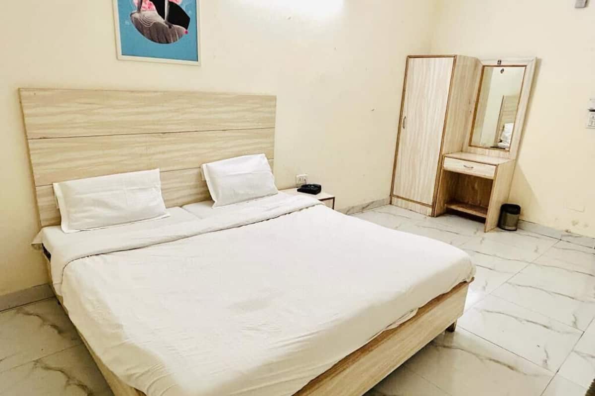 Quarto com cabeceira de madeira, cama com roupa de cama branca, mesa de cabeceira, guarda-roupa e espelho.