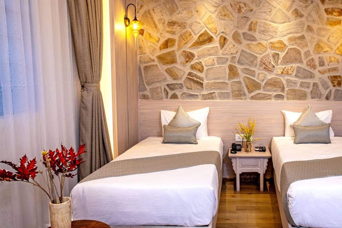 Quarto com duas camas, uma parede de pedra e uma mesa de cabeceira com abajur.