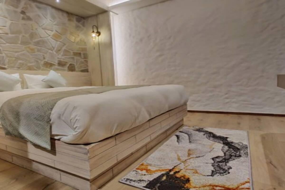 Quarto com parede de pedra, cama com roupa de cama branca e tapete estampado.