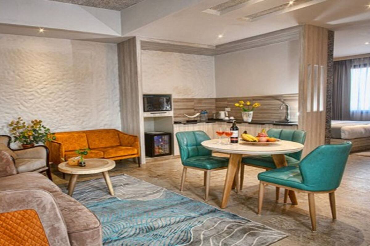 Uma sala moderna com sofá, mesa de centro e cadeiras, área de cozinha com mesa de jantar e uma cama ao fundo.