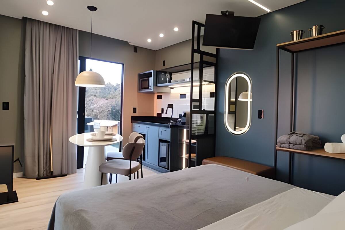 Quarto de hotel moderno com uma cama grande, área de refeições e cozinha compacta.