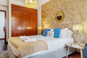 Quarto de hotel com uma cama grande, um guarda-roupa, um espelho redondo e duas luminárias de cabeceira.