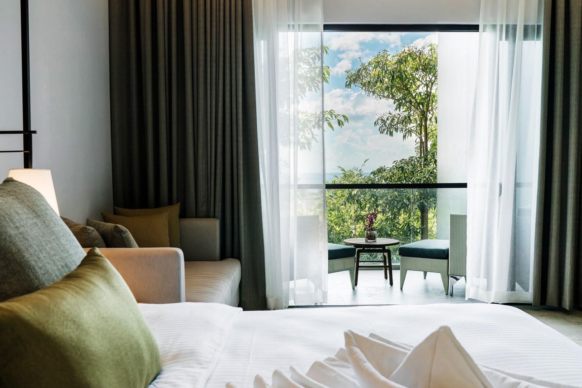 Quarto de hotel com uma cama grande, um sofá e uma varanda com mesa e cadeiras.