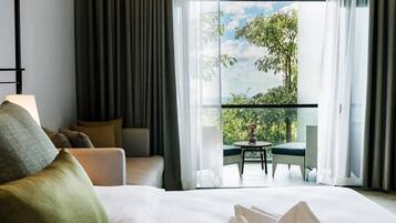 Quarto de hotel com uma cama grande, um sofá e uma varanda com mesa e cadeiras.