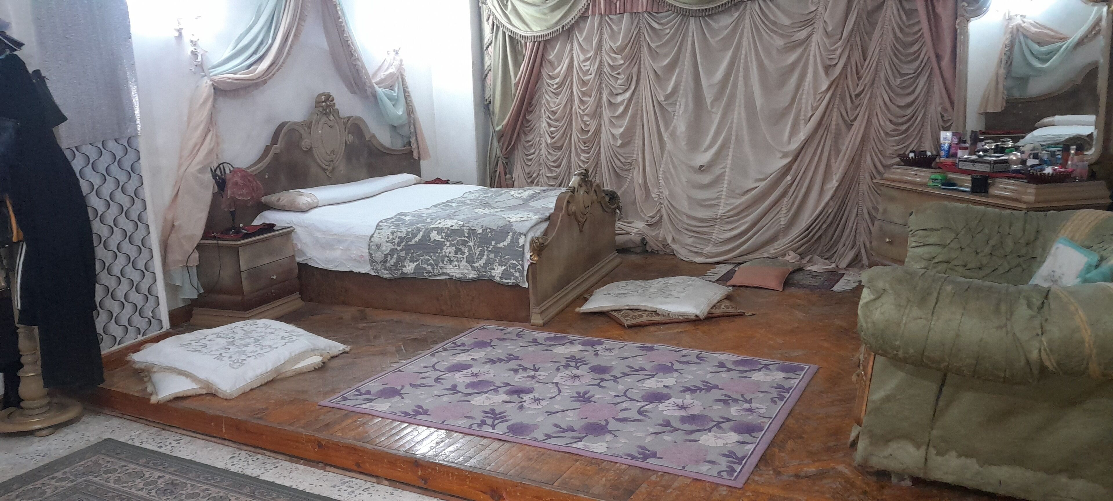 Um quarto com uma cama de madeira, um tapete floral, uma poltrona verde e uma mesa de cabeceira com abajur.