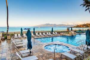 Uma área de piscina com espreguiçadeiras e guarda-sóis, uma banheira de hidromassagem e vista para o oceano e montanhas.