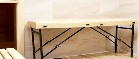 Um quarto com um banco de madeira, uma mesa com estrutura de metal preto e uma parede revestida de azulejos.