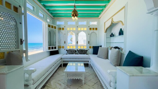 Quarto com sofá branco, uma mesinha e vista para o mar.