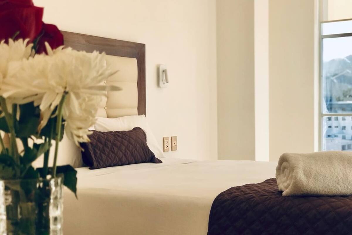 Quarto de hotel com cama, um vaso com flores brancas e uma janela com vista.