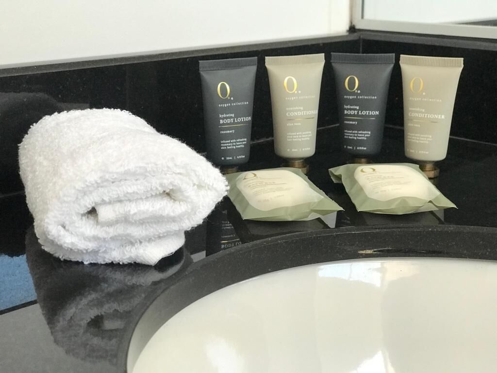 Uma bancada de banheiro com uma toalha branca, quatro frascos de loção corporal e dois pequenos sachês.