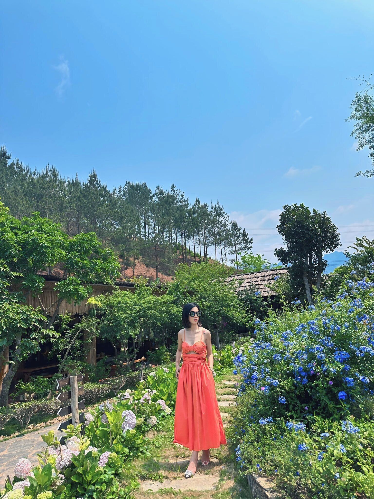 Uma mulher de vestido vermelho está em um jardim com diversas plantas e flores.