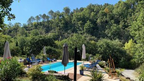 Área de piscina com espreguiçadeiras e guarda-sóis, cercada por vegetação exuberante.