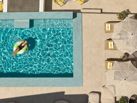 Piscina com uma pessoa flutuando em um boi de borracha, cercada por espreguiçadeiras e guarda-sóis.