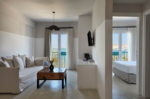 Quarto de hotel moderno com sofá, mesa de centro, TV na parede e varanda vista para o mar.