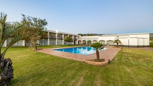 Um edifício moderno com piscina, cercado por gramado bem cuidado e palmeiras.
